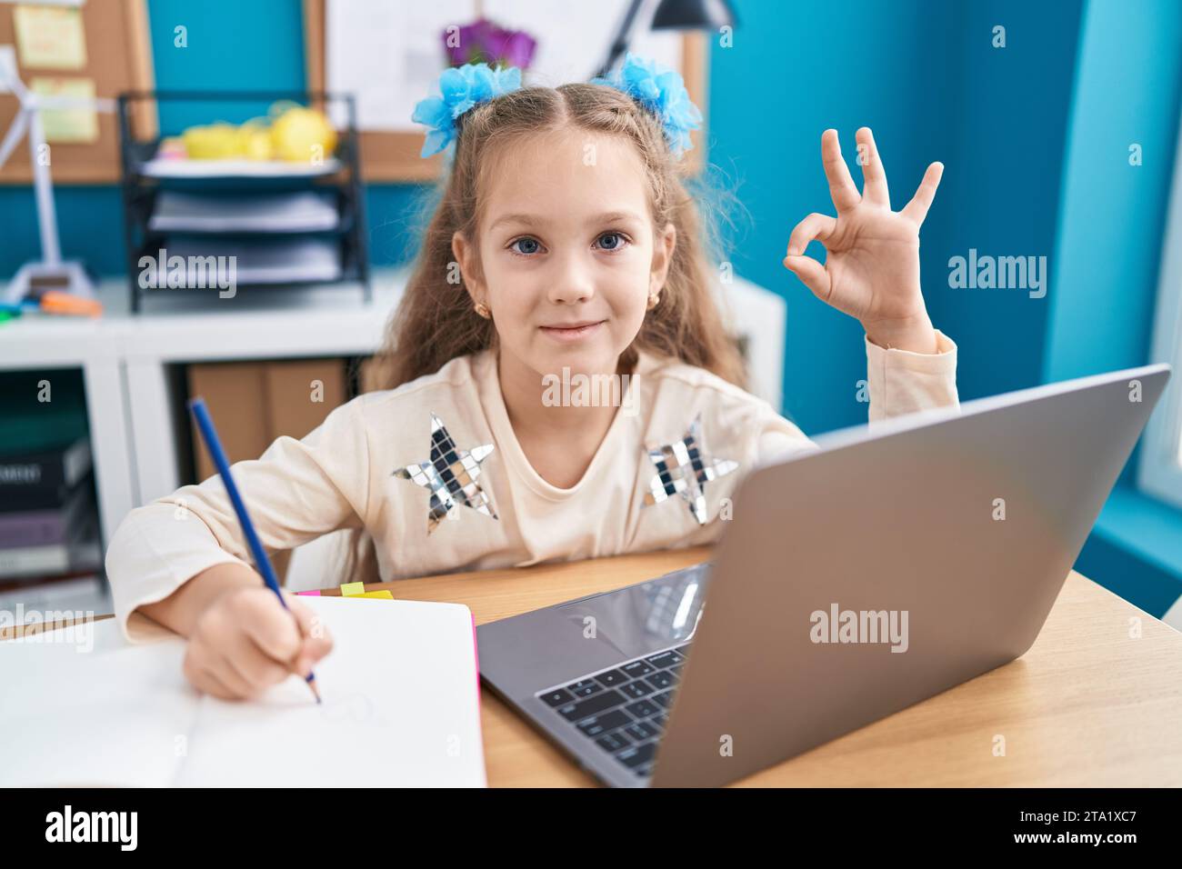 Young little girl sitting on the table doing homework with laptop doing ...