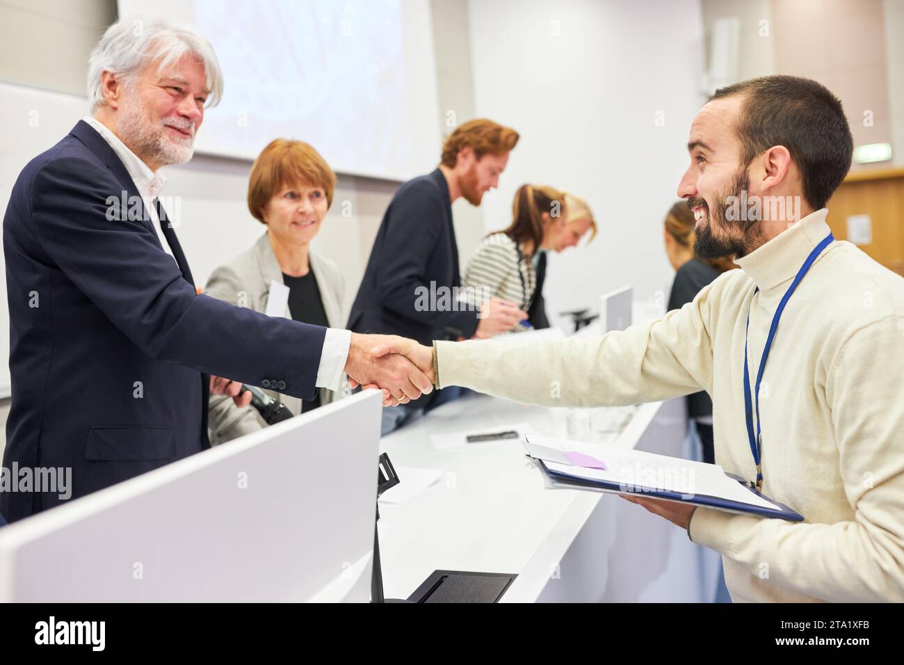 Male speaker handshaking with smiling professional at stage during ...