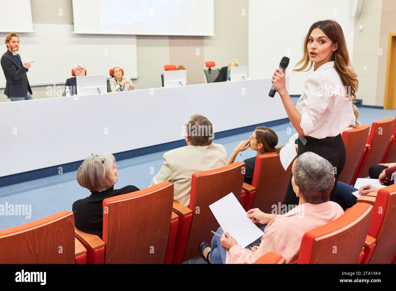 Portrait of female professional standing in audience asking question to ...