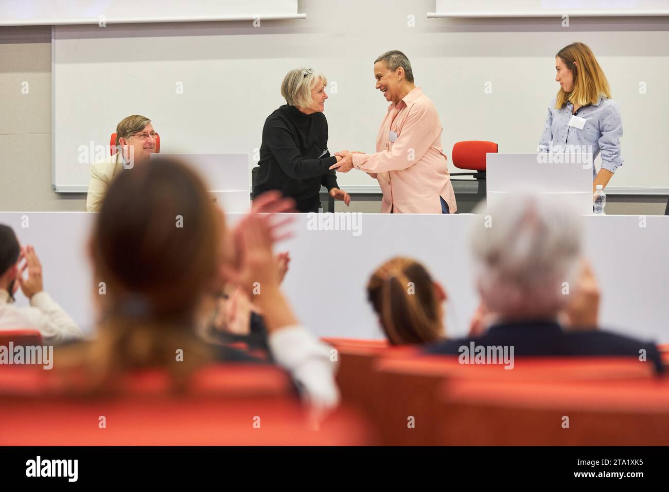 Female professionals handshaking on stage in front of audience at ...