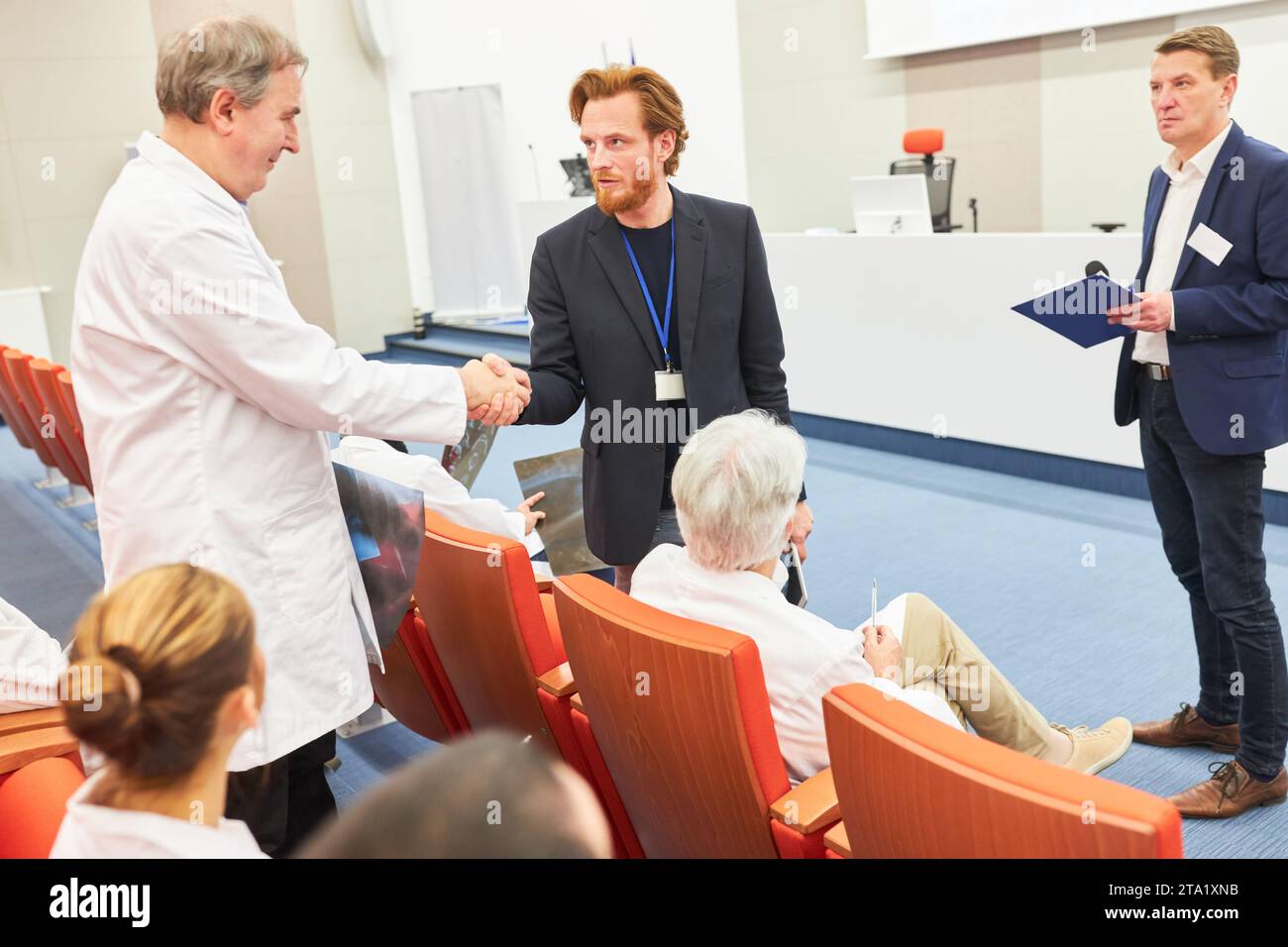 Male doctor in audience of medical conference handshaking with speaker ...