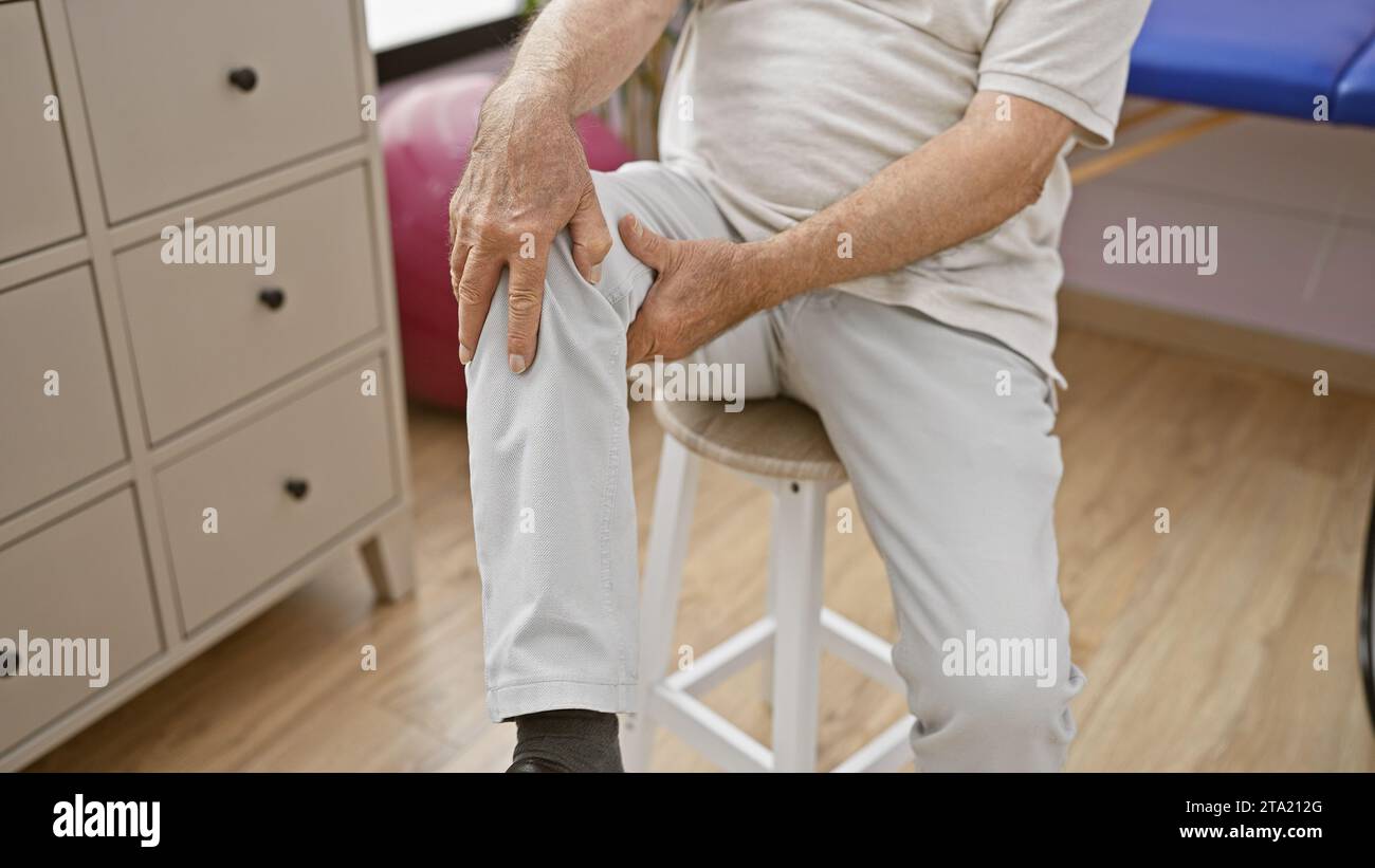 Senior man's hands touch knee in pain, suffering in rehab clinic during ...