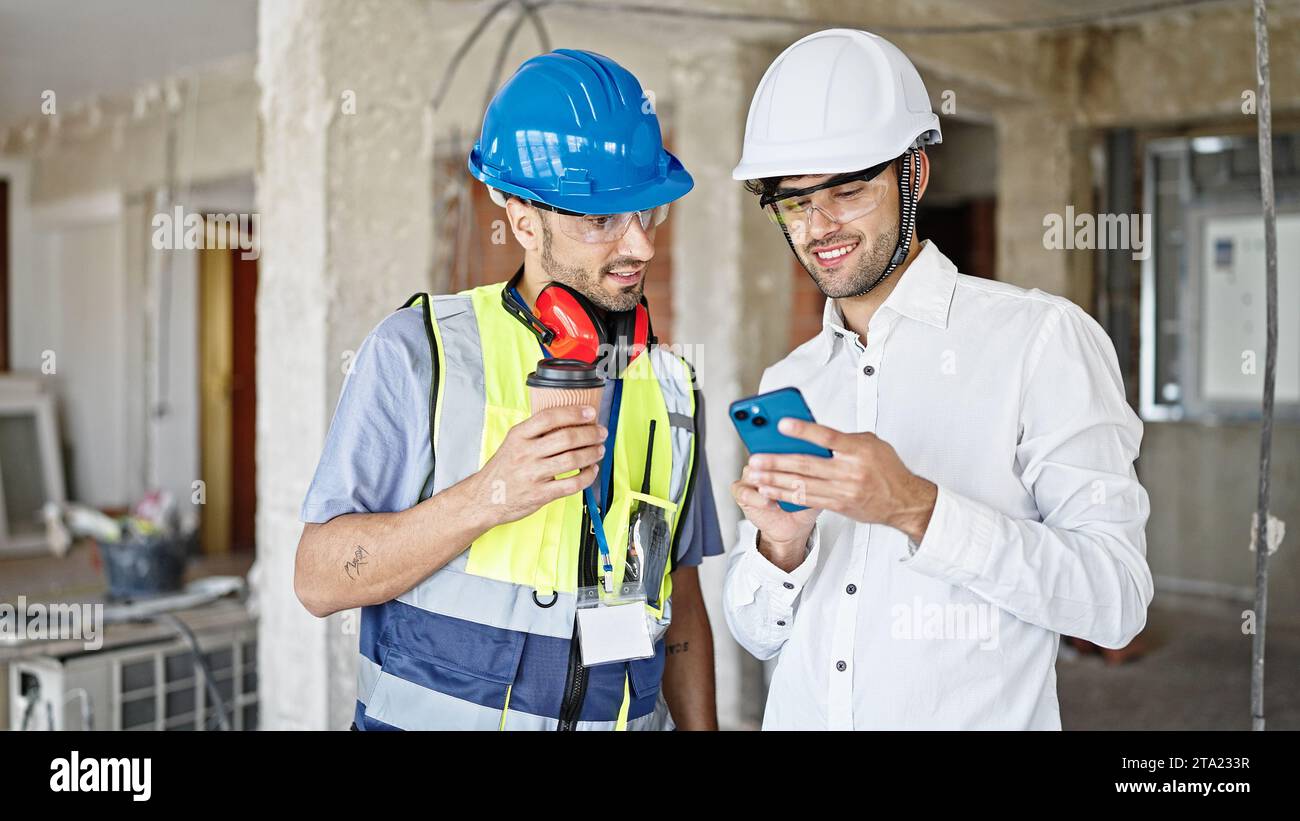 Two men builder and architect using smartphone drinking coffee at ...