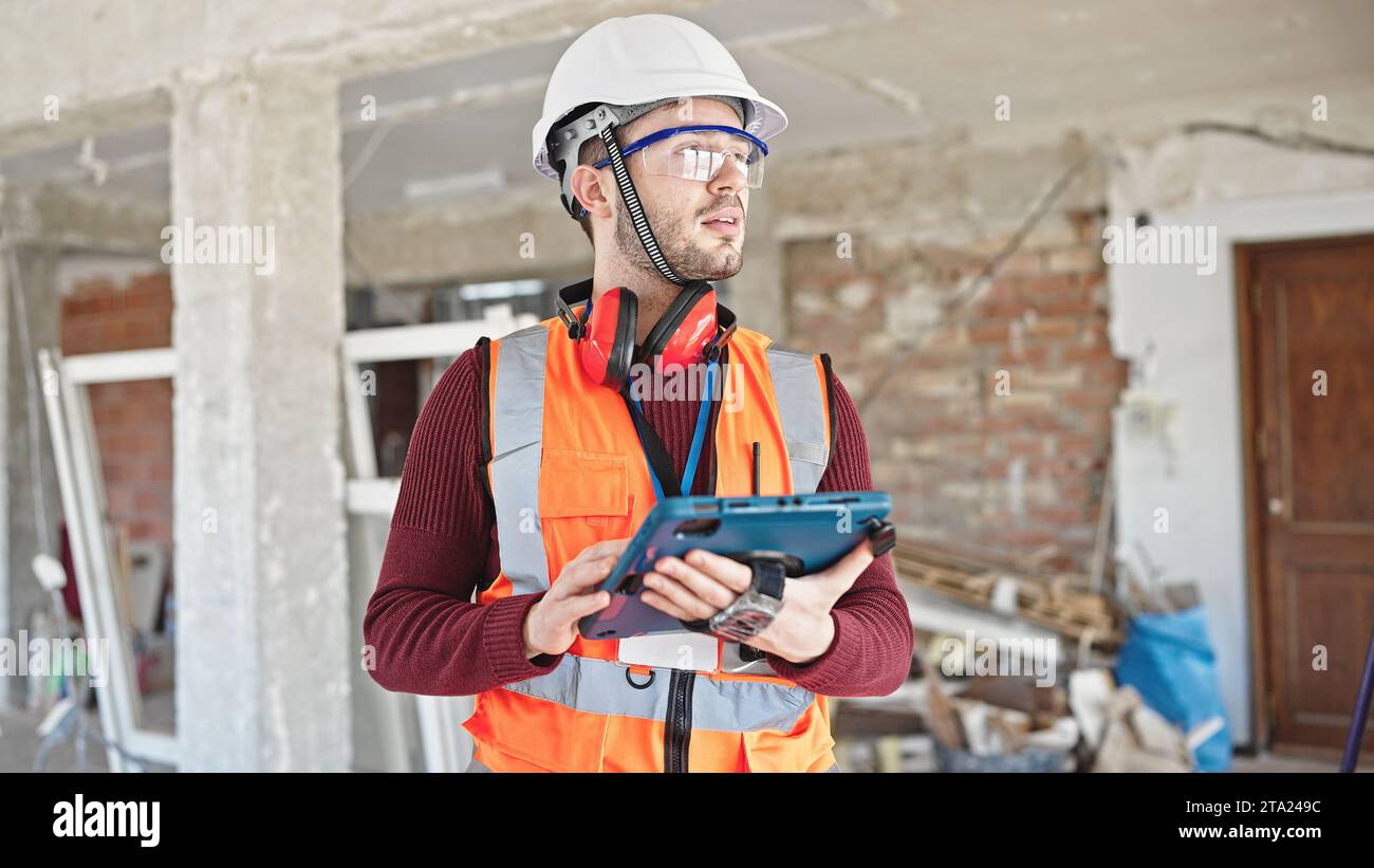 Young hispanic man builder using touchpad looking around at ...