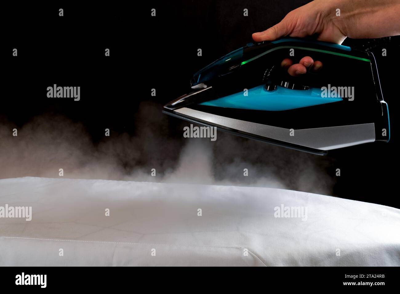 Woman ironing a white cloth by pouring steam from the iron on a black ...