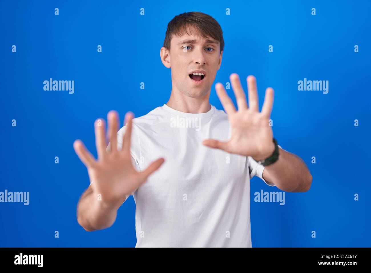 Caucasian blond man standing over blue background afraid and terrified ...