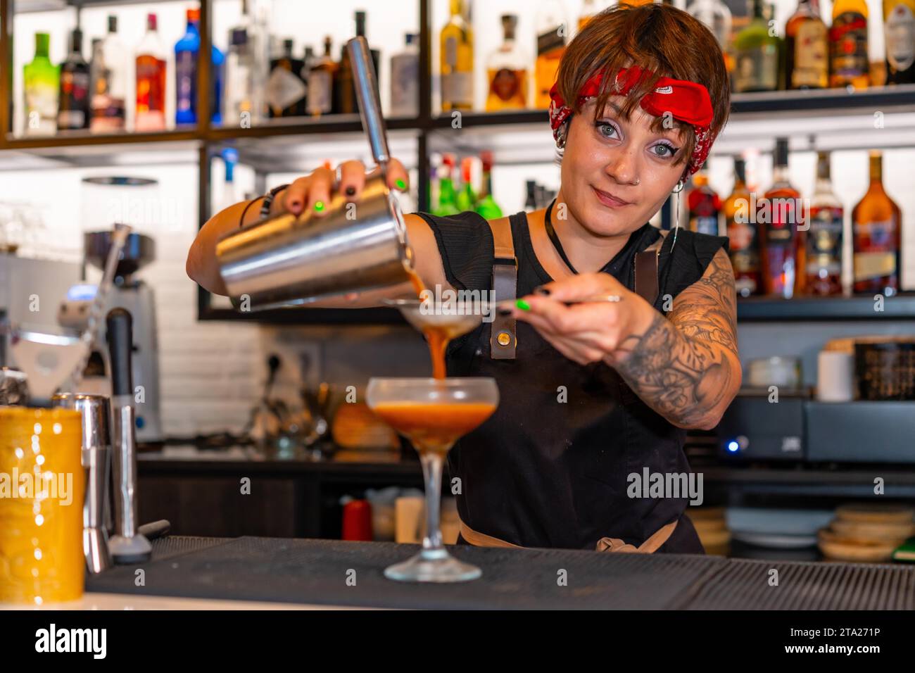 Happy bartender pouring cocktail from the shaker into a cocktail glass ...
