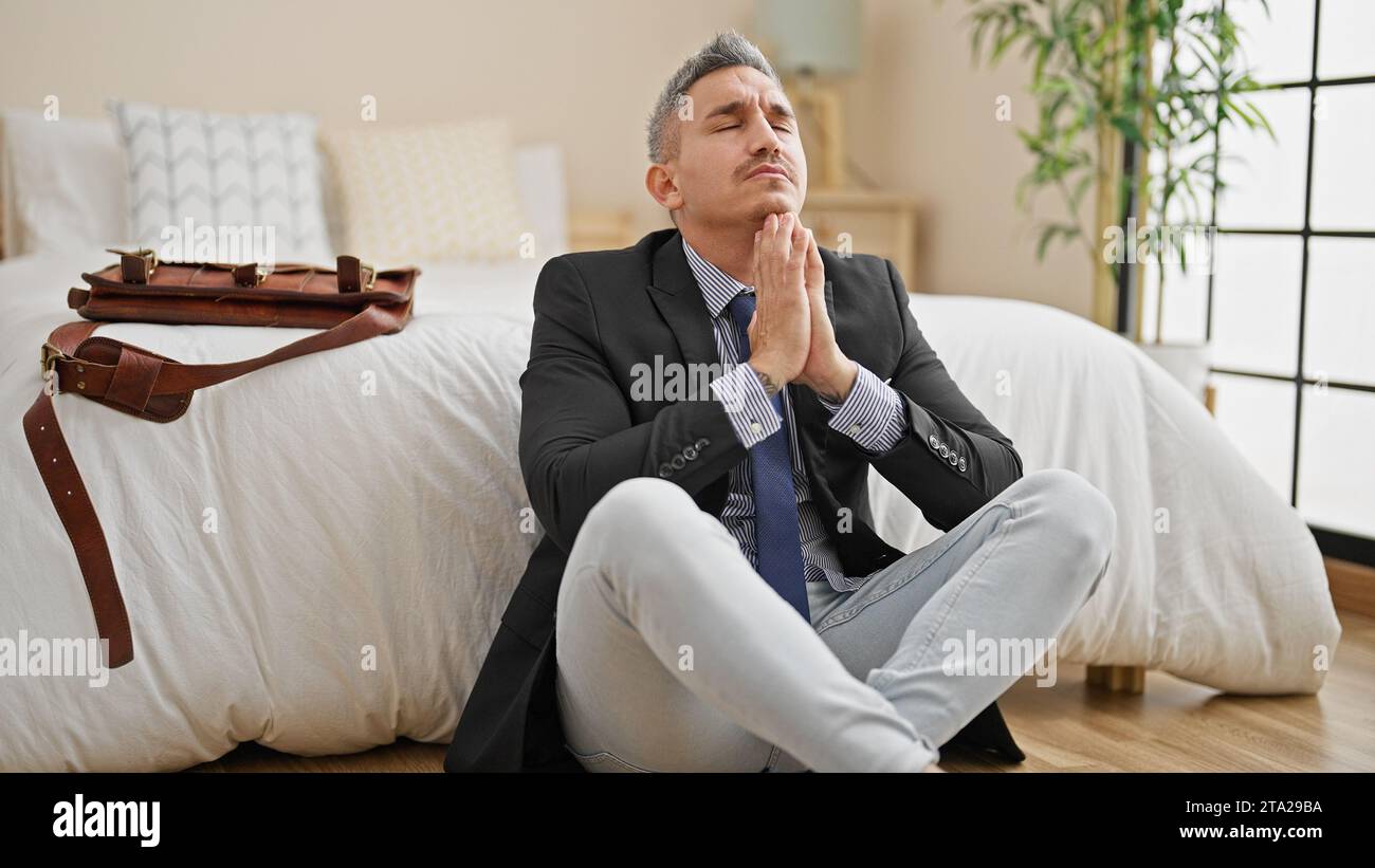 Young hispanic man business worker praying sitting on floor at hotel ...