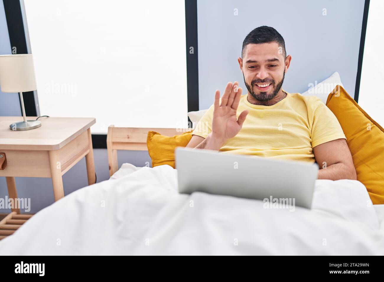 Hispanic man using laptop on the bed looking positive and happy ...