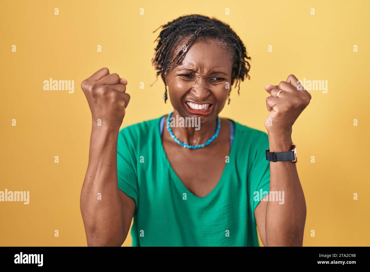 African woman with dreadlocks standing over yellow background angry and ...