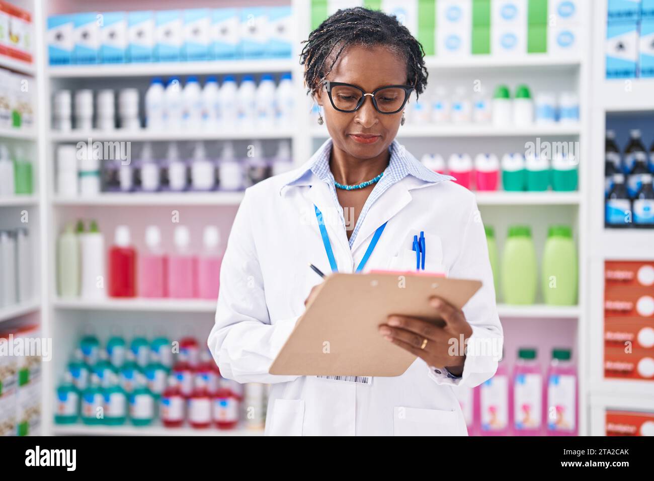 Middle age african american woman pharmacist writing on document at ...