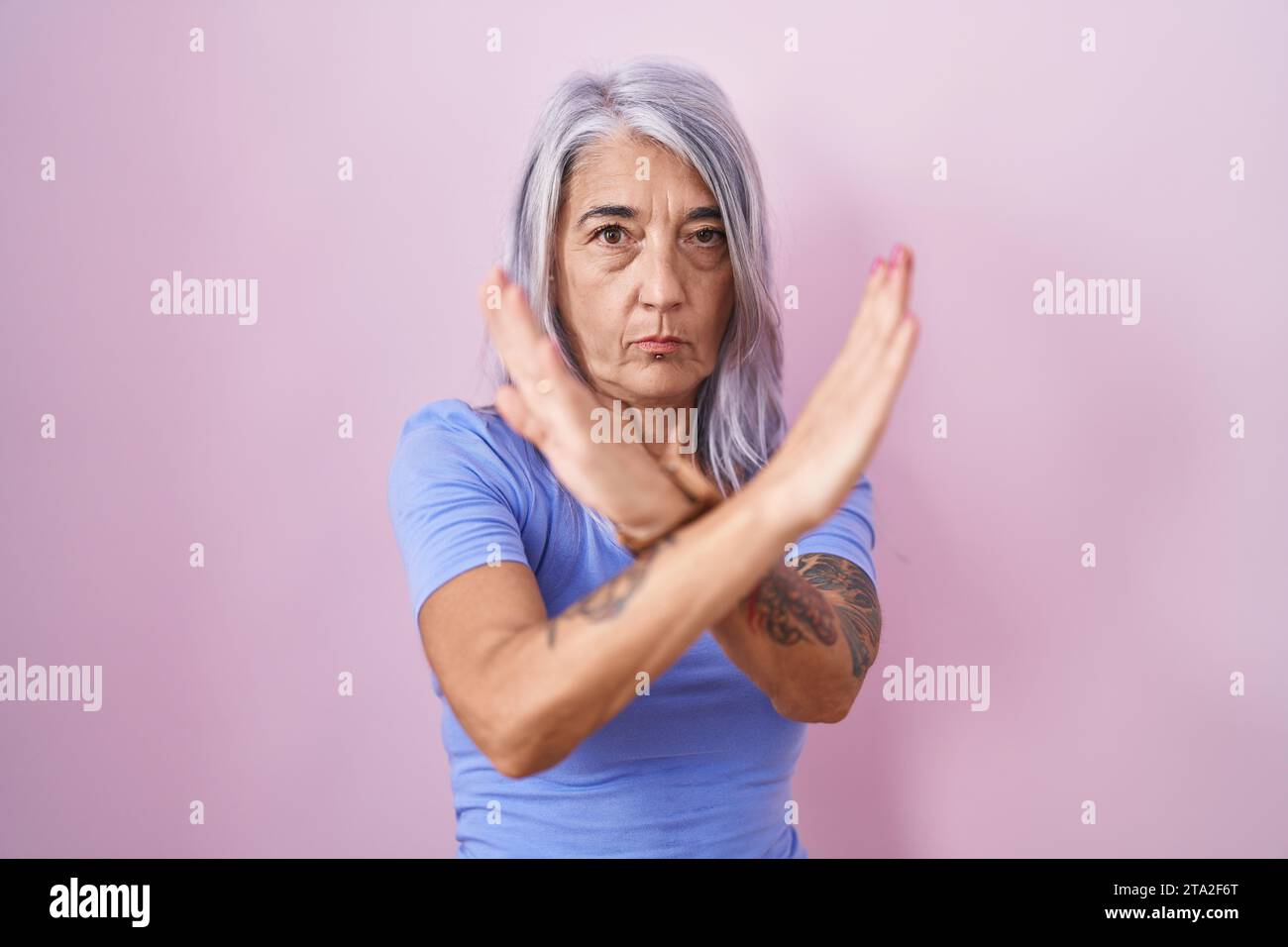Middle age woman with tattoos standing over pink background rejection ...