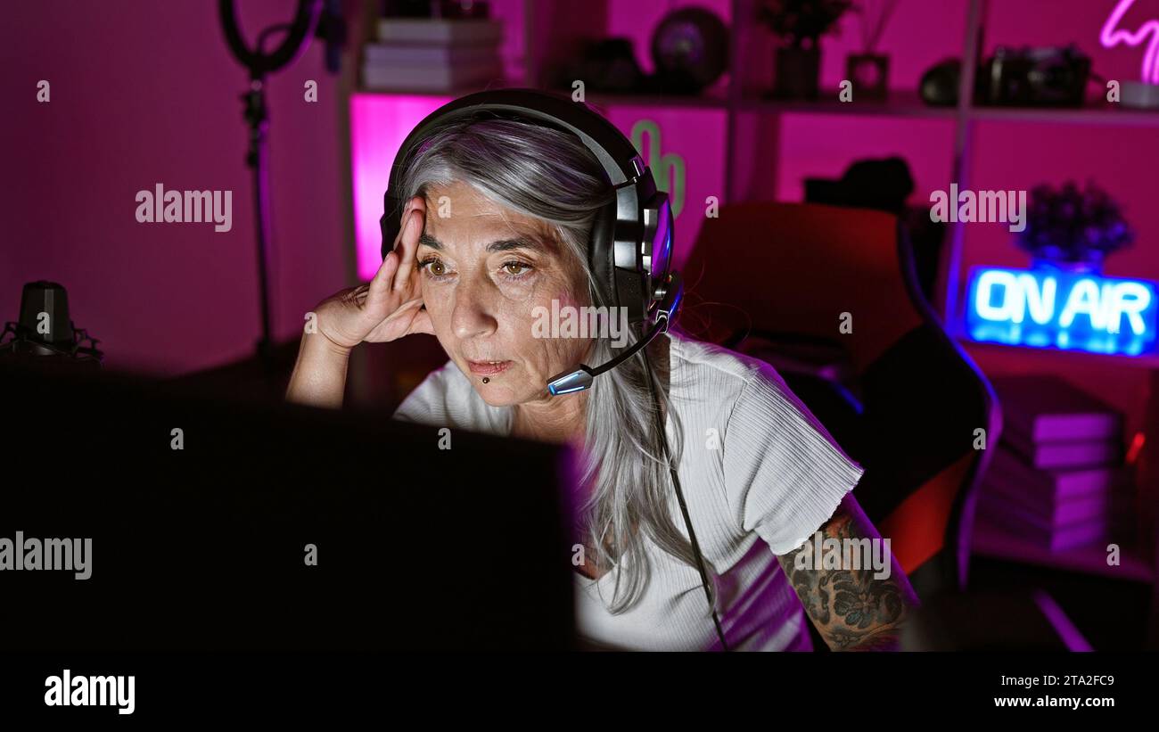 Mature, grey-haired woman gamer, in serious gaming mode, streaming live ...