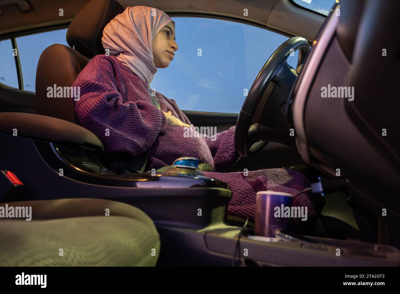 Pregnant arabic muslim woman driving car at night wearing winter ...