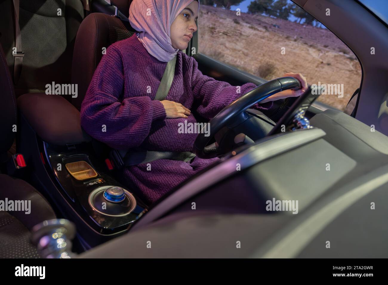 Pregnant arabic muslim woman driving car at night wearing winter ...