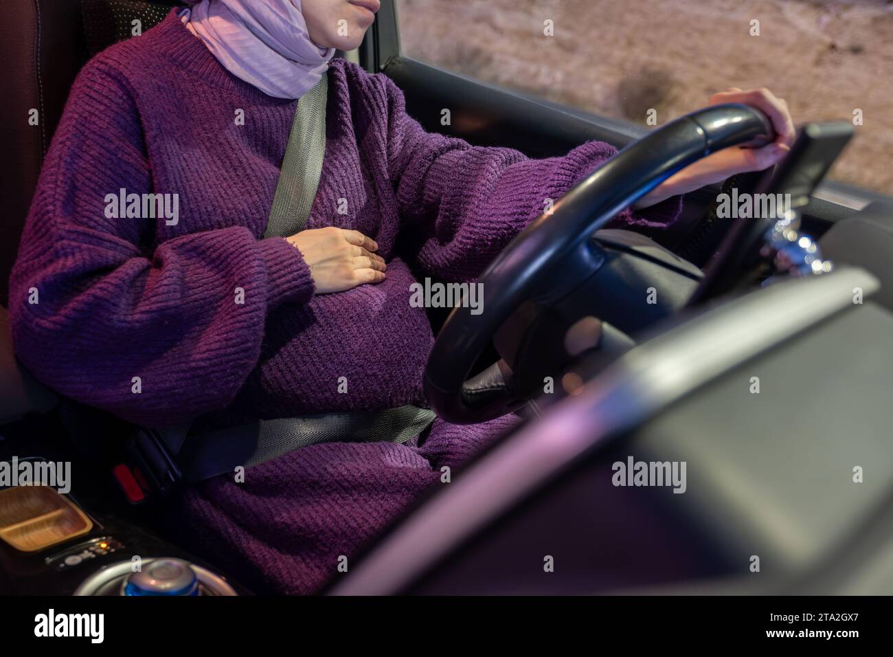 Pregnant arabic muslim woman driving car at night wearing winter ...