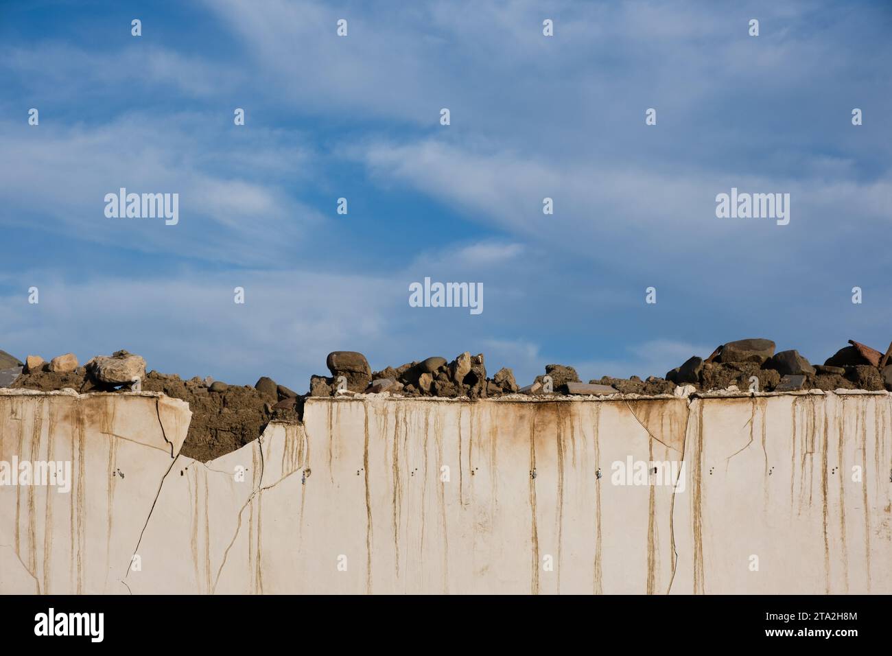 Clay damaged collapsing wall against blue cloudy sky. Deserted places ...