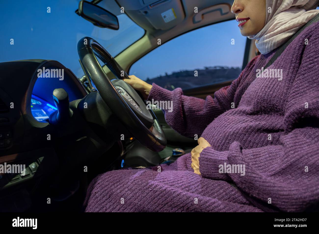 Pregnant arabic muslim woman driving car at night wearing winter ...