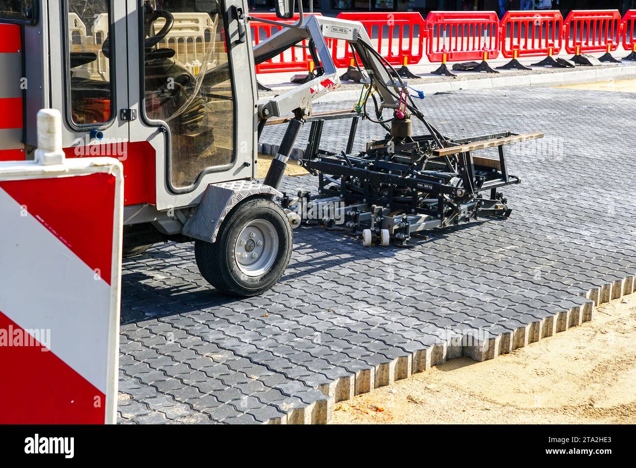 Paving block laying machine on new pavement, red plastic barriers ...