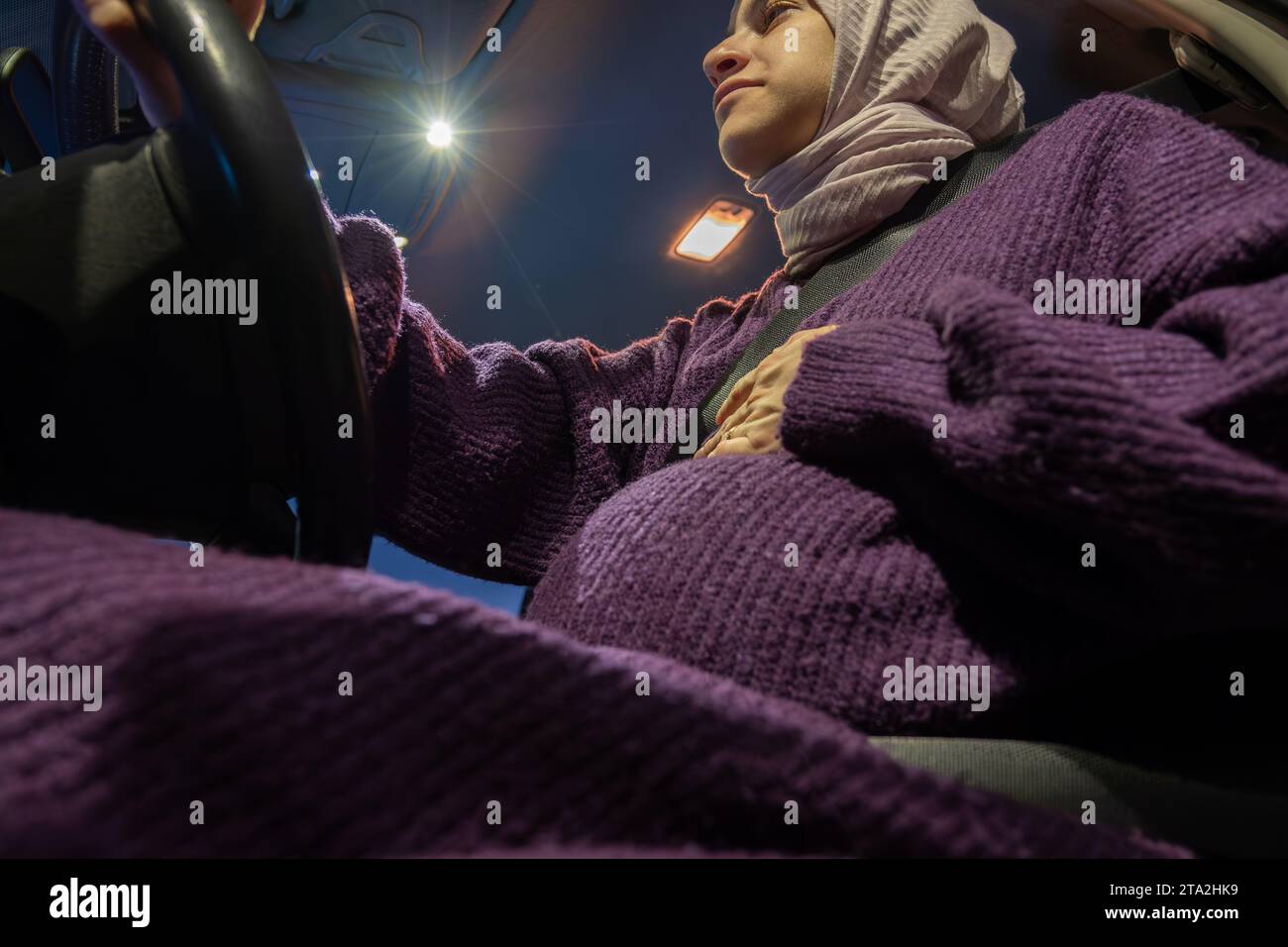 Pregnant arabic muslim woman driving car at night wearing winter ...
