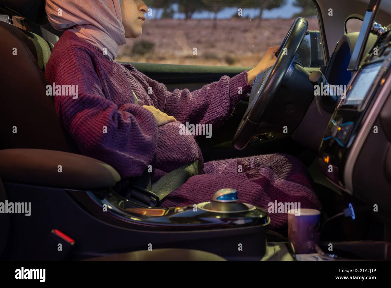 Pregnant arabic muslim woman driving car at night wearing winter ...