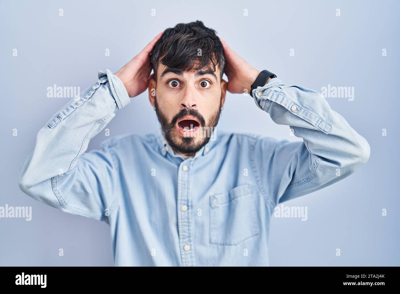 Young hispanic man with beard standing over blue background crazy and ...