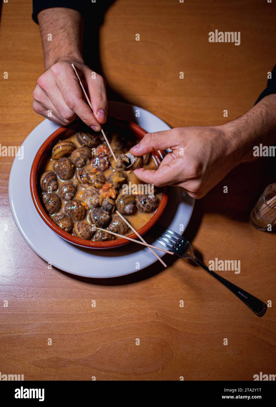 OVERVIEW OF SNAILS DISH IN SAUCE IN A CLAY POT. SOMEONE IS EATING ONE ...