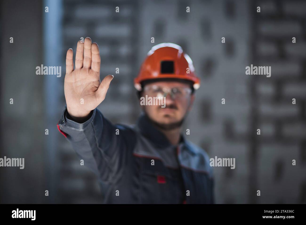 A worker in overalls and a hard hat shows an open palm demonstrating a ...