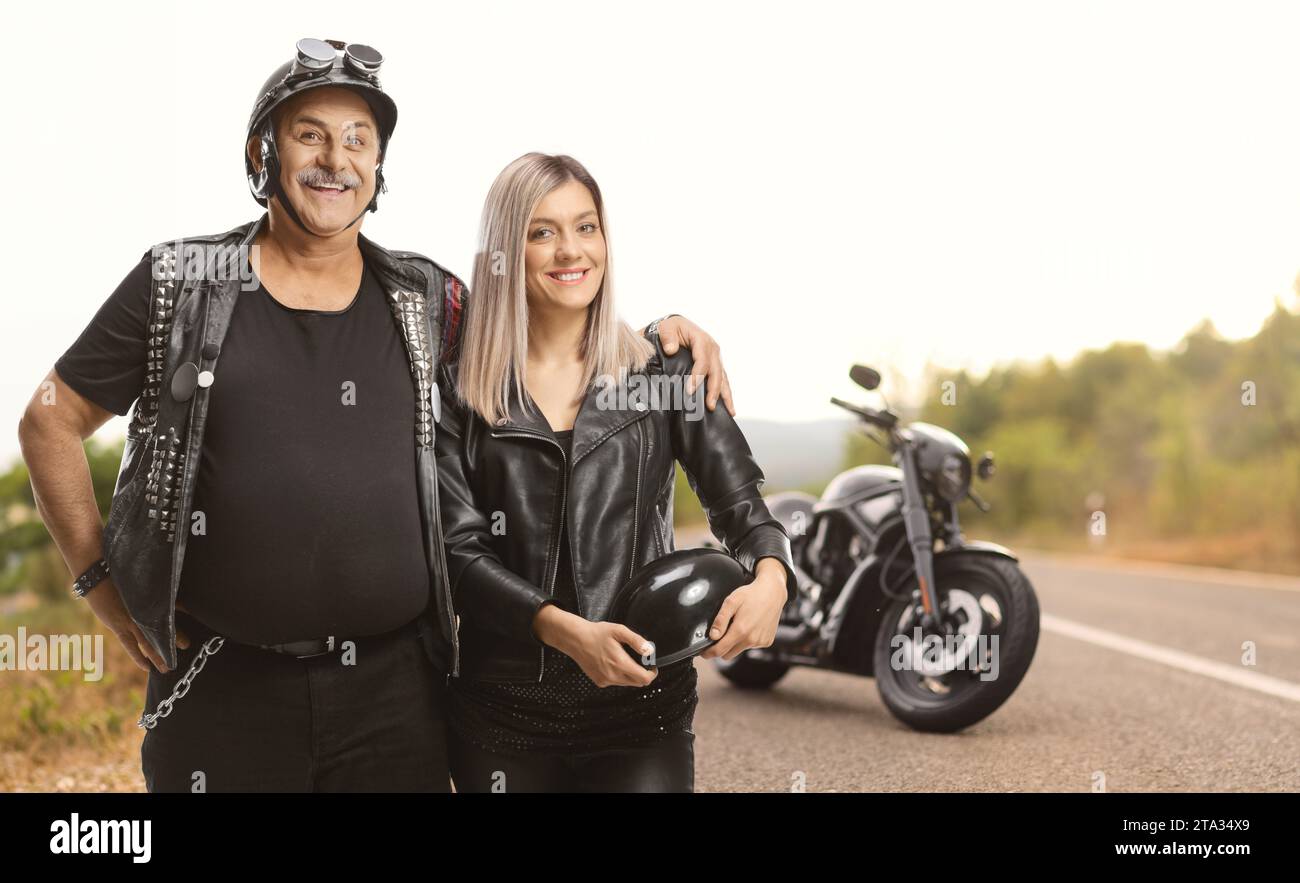 Elderly biker with a young woman in leather clothes posing on the road ...