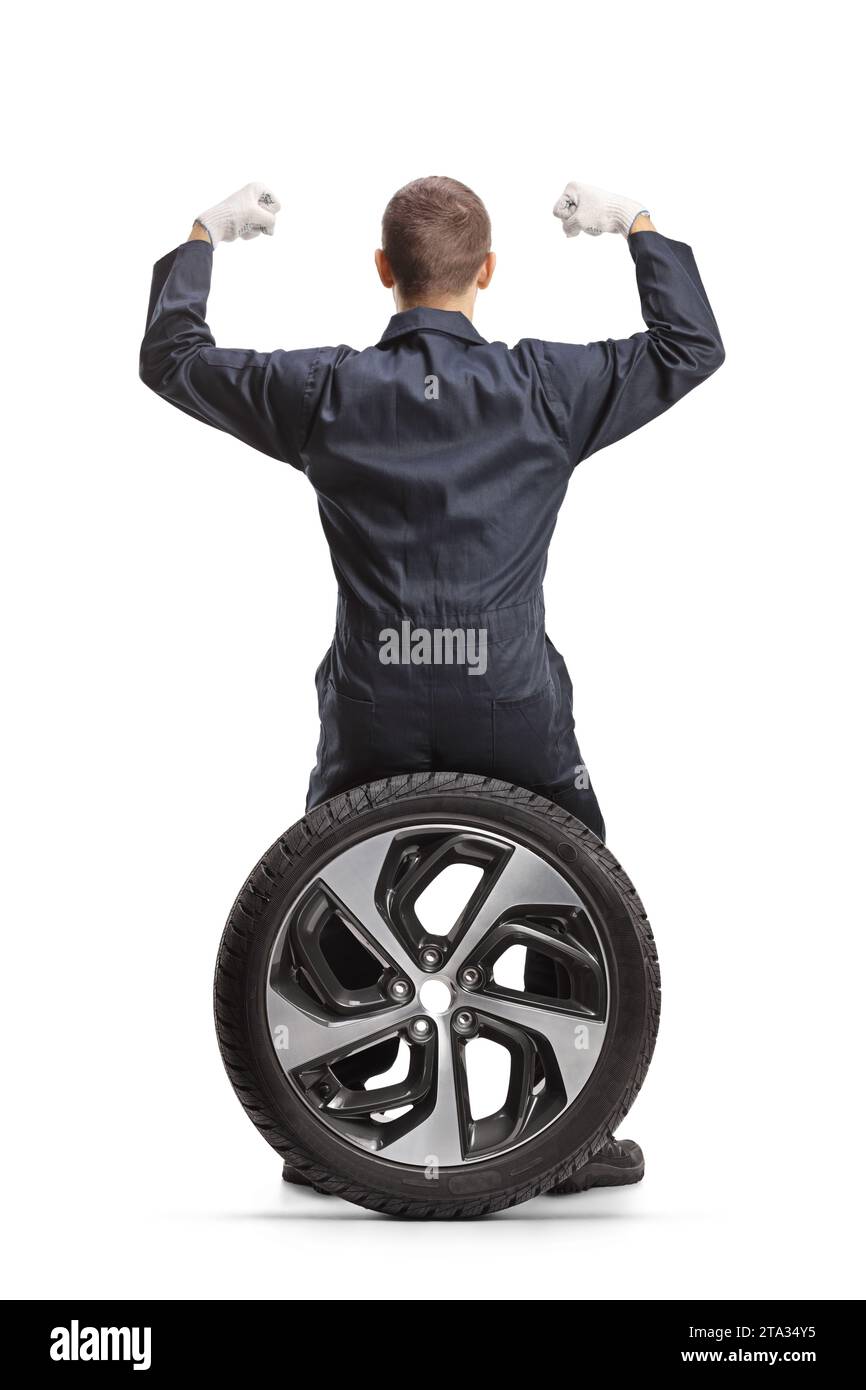 Rear view shot of a car mechanic sitting on a tire and flexing muscles ...