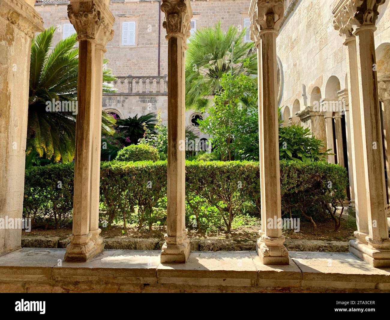 An idyllic courtyard featuring impressive columns and lush green bushes ...