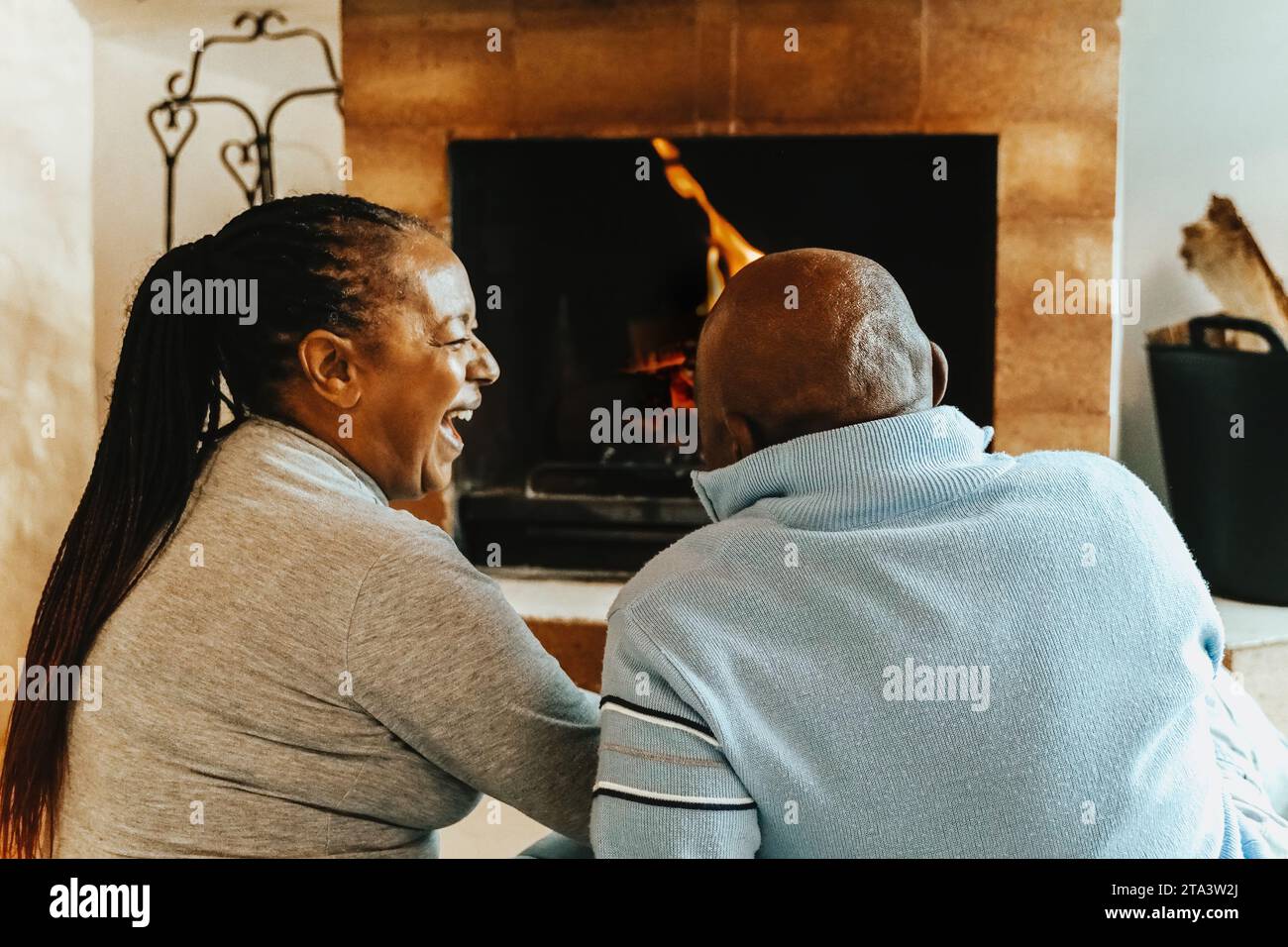 Senior African couple by cozy fireplace having fun together inside ...