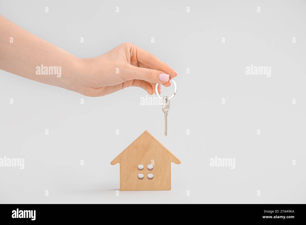 Female hand with wooden house figure and key on grey background ...