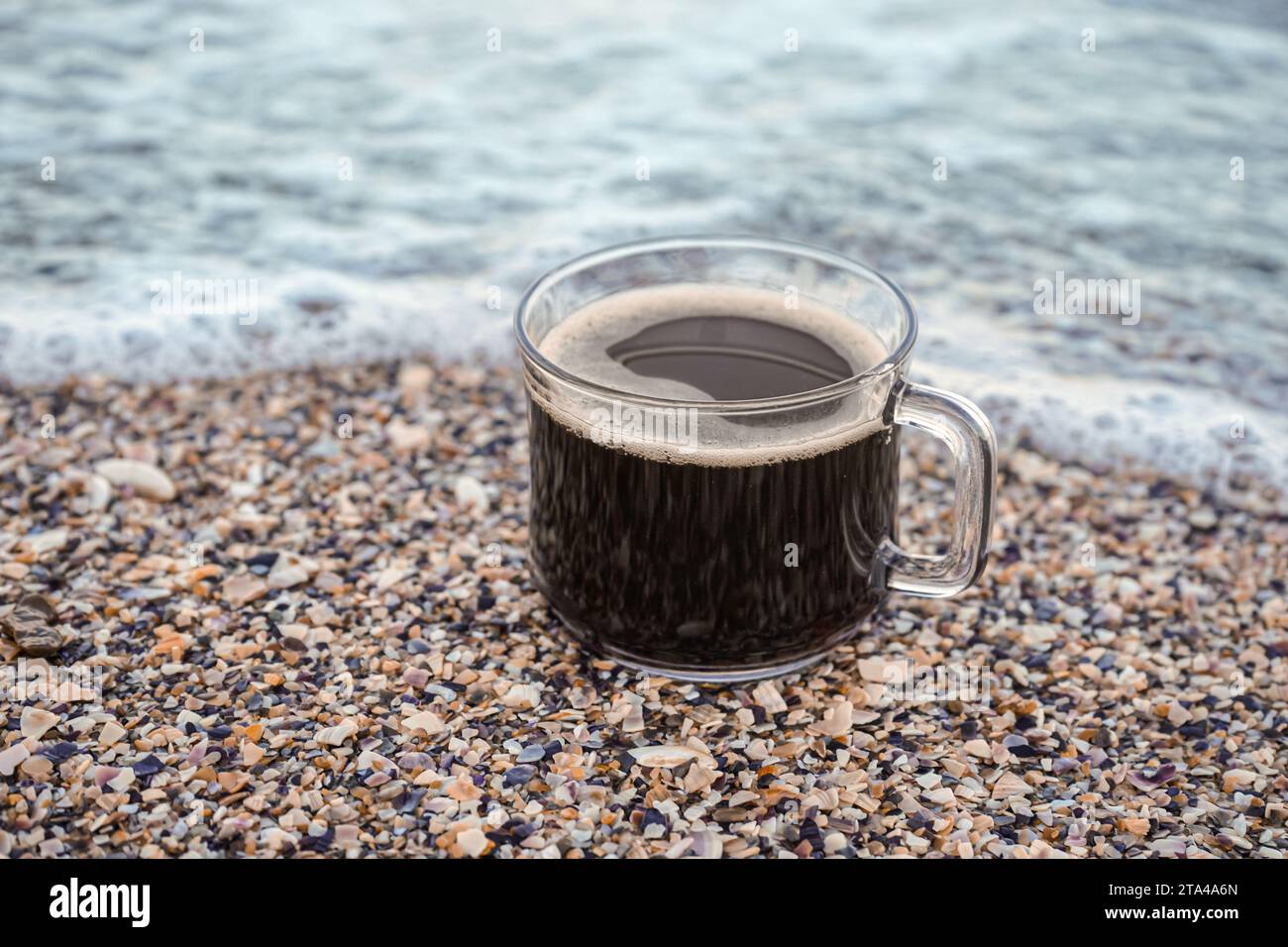 Glass mug of coffee on pebble beach Stock Photo - Alamy