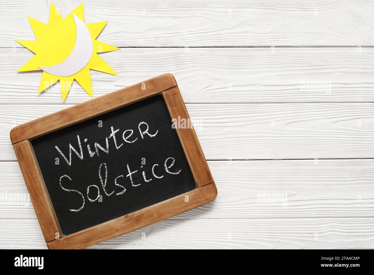 Chalkboard with text WINTER SOLSTICE and paper sun on white wooden ...