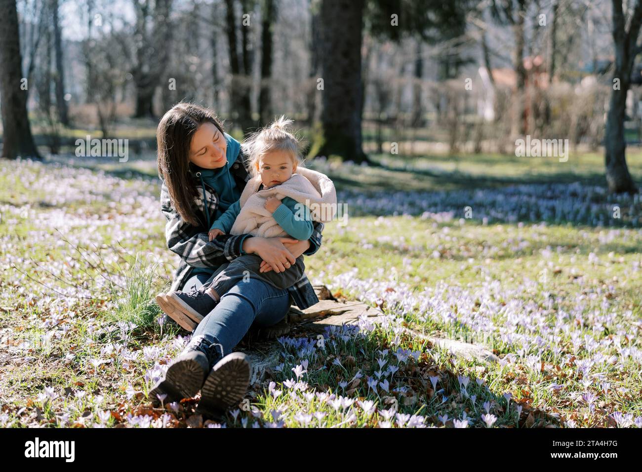 Mom looks at a little girl on her knees sitting on a stump in a ...