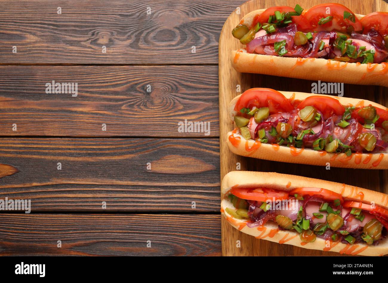 Tasty hot dogs with green onion, tomato, pickles and sauce on wooden ...