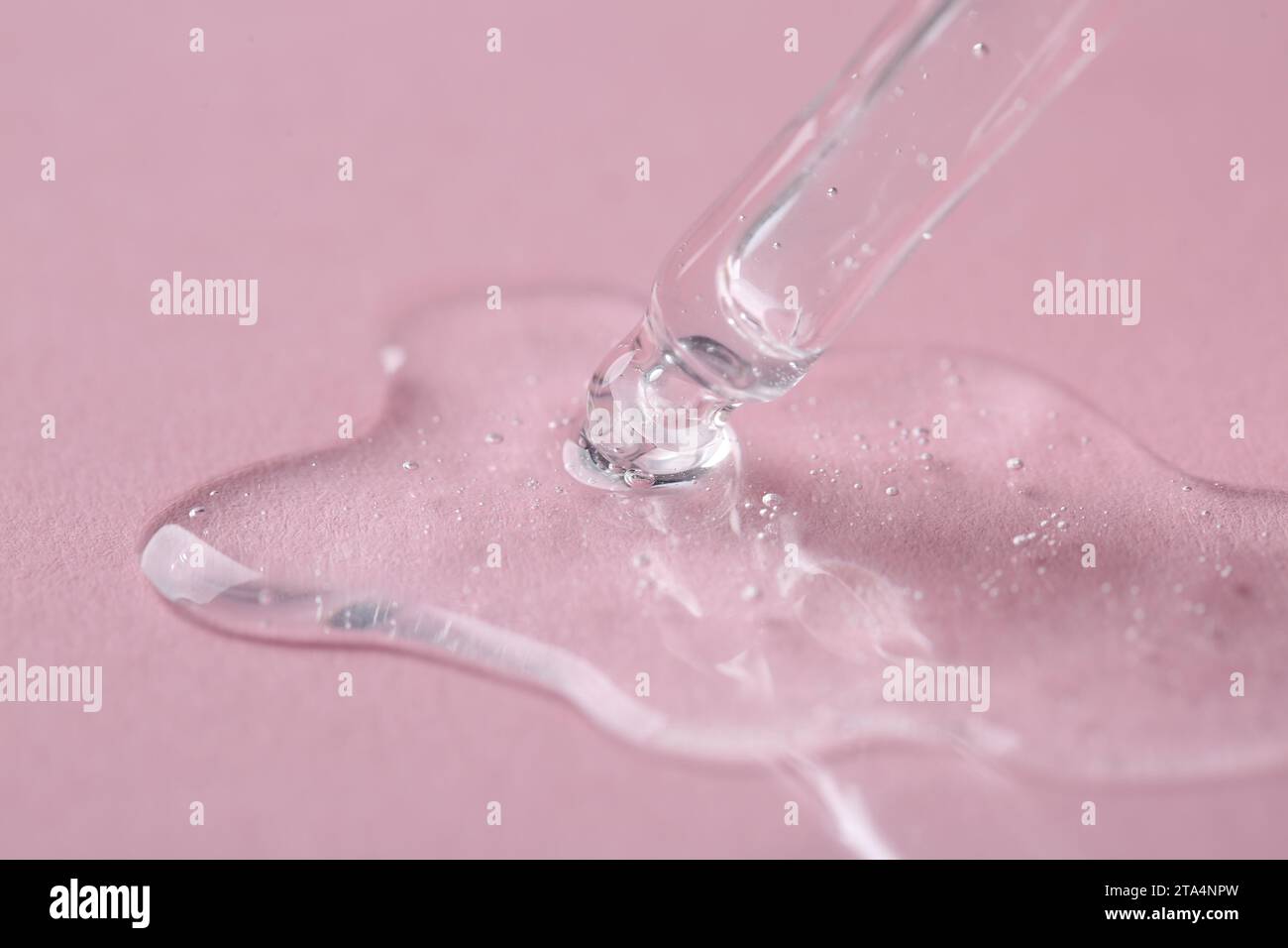 Dripping cosmetic serum from pipette onto pink background, macro view ...