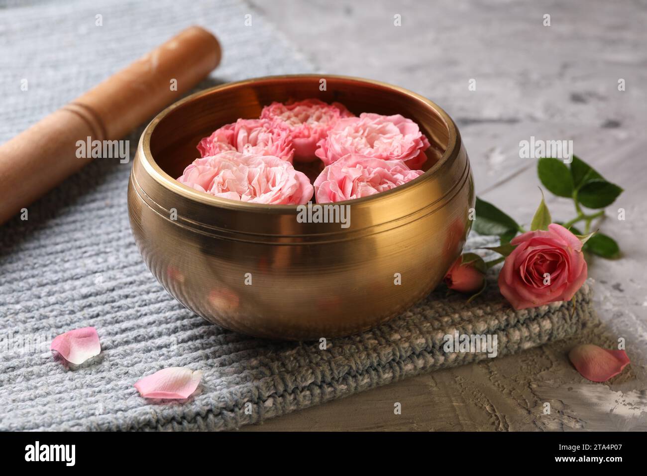 Tibetan singing bowl with water, beautiful roses and mallet on grey ...