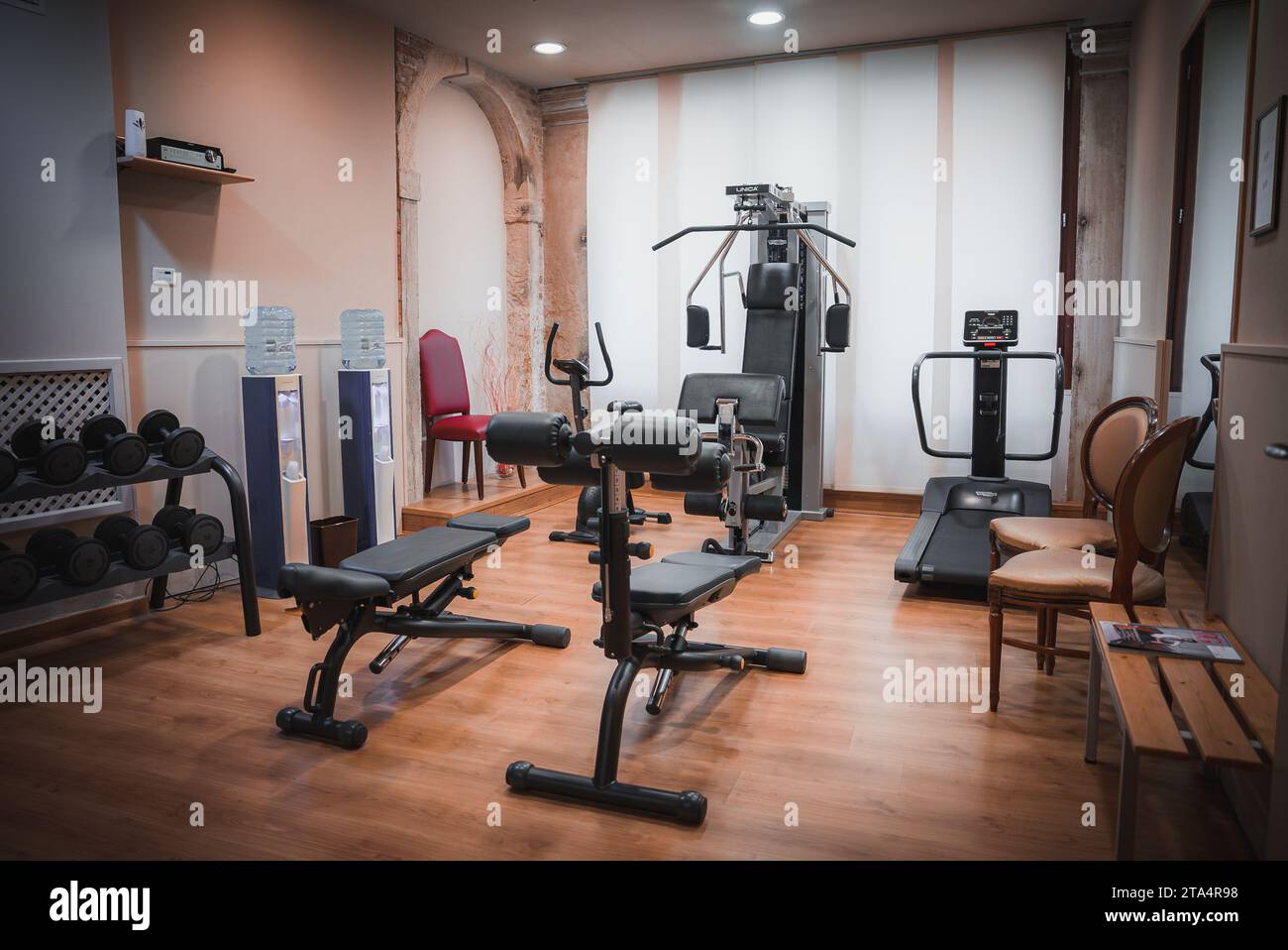 Modern gym room with rowing machine, exercise equipment, and chair in ...
