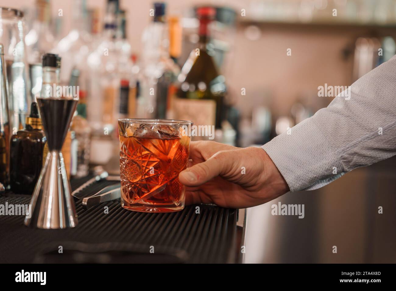 Elegant bartender pouring vibrant red drink into martini glass, showcasing precision and ...