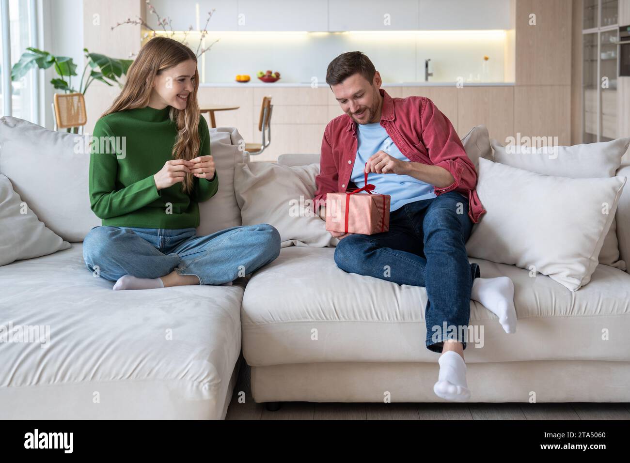 Tenderly loving female looking at boyfriend unbracing ribbon on giftbox ...