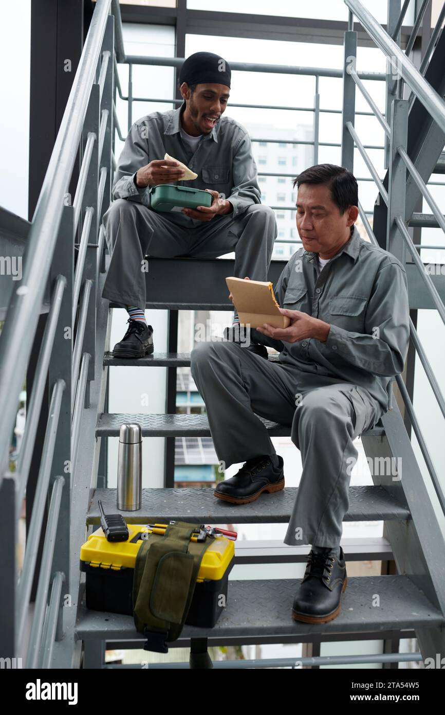 Hungry construction workers sitting on steps and eating sandwiches with ...