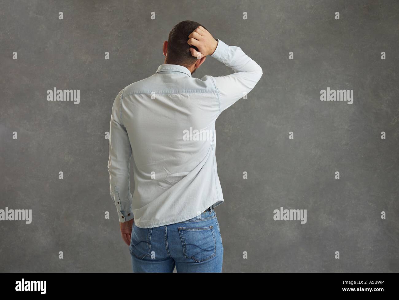 Unknown man stands with his back to the camera and scratches the back ...