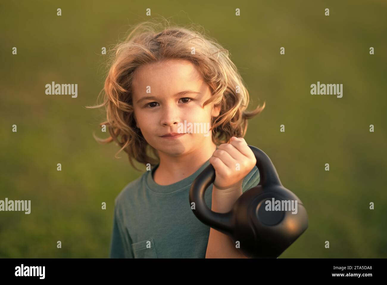 Child lifting the kettlebell in park outside. Child boy pumping up ...
