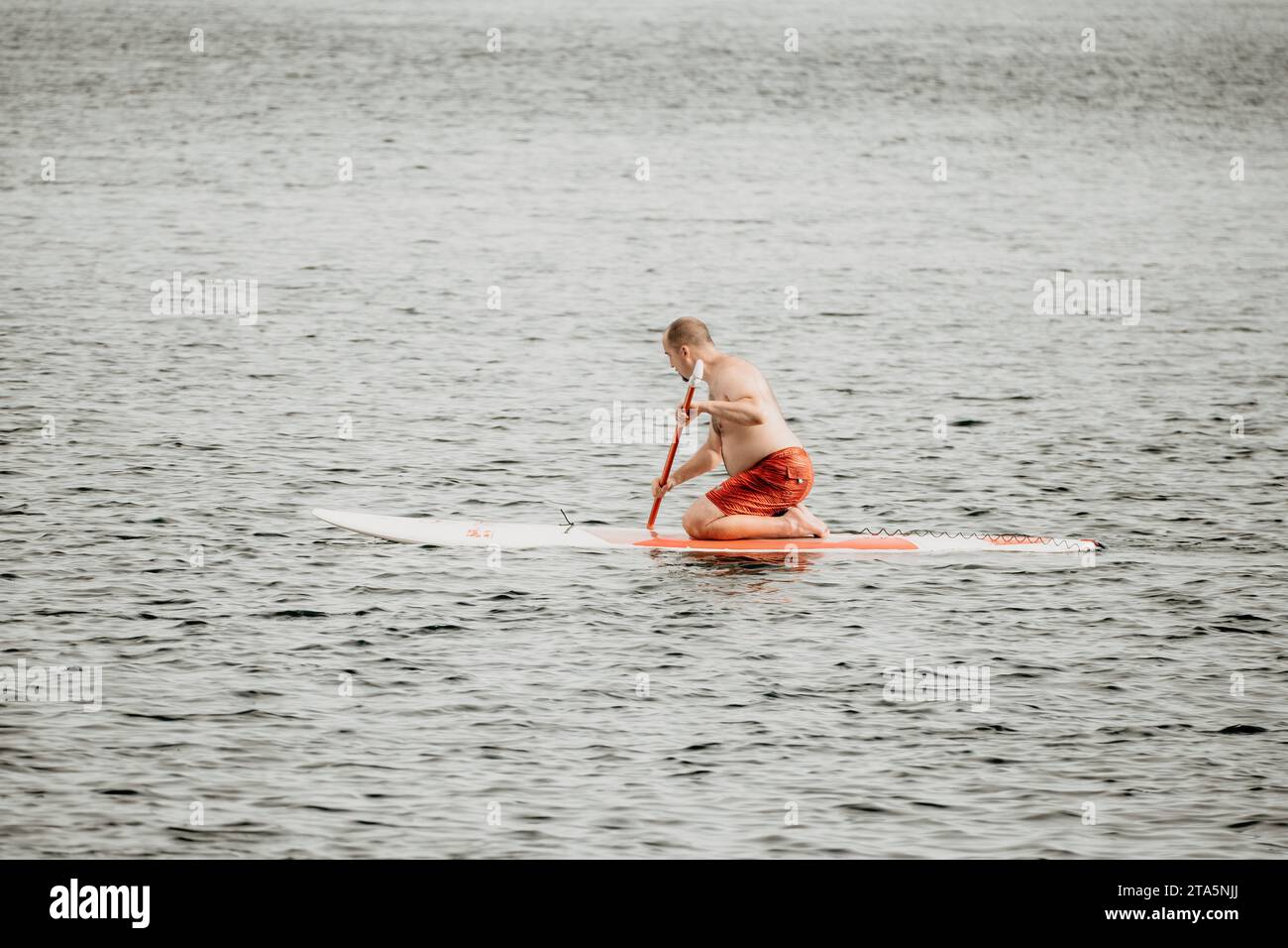 Active mature male paddler with his paddleboard and paddle on a sea at summer. Happy senior man ...