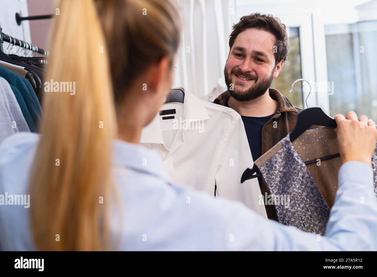 Saleswoman presenting a shirt to a male customer who is examining a ...