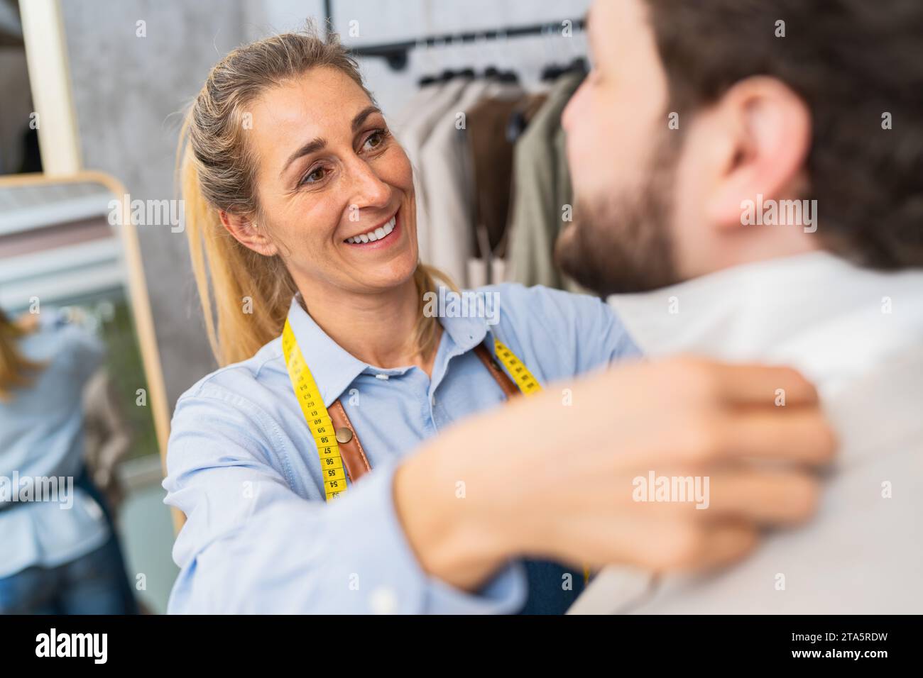 Tailor woman fitting a shirt on a male client, both smiling in a shop ...