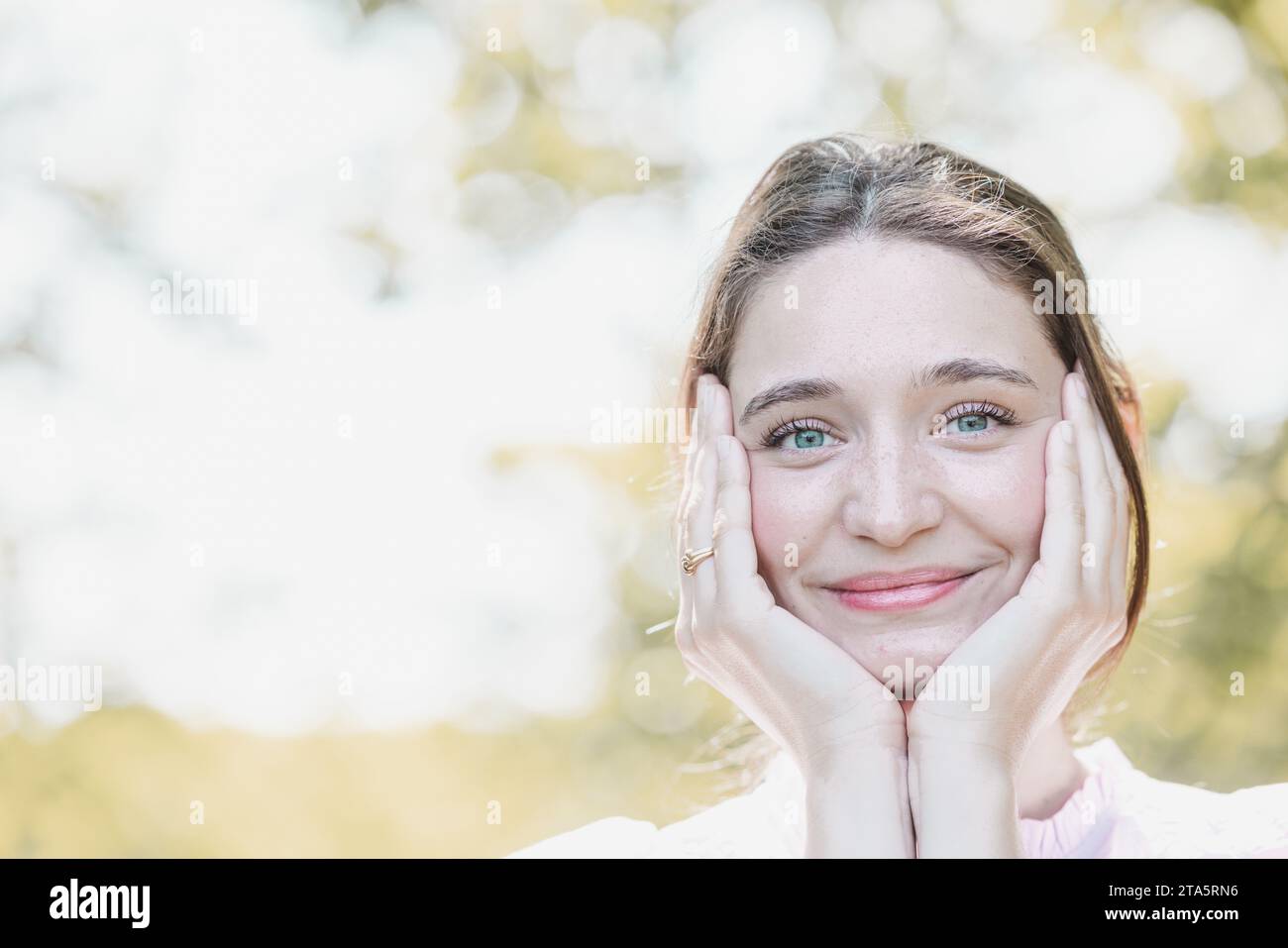 A young woman is pictured with a radiant smile, hands delicately ...