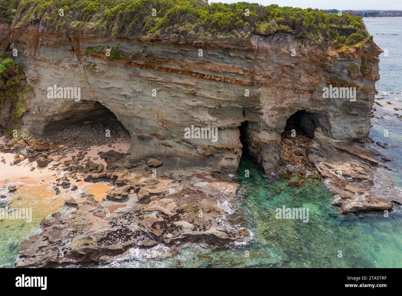Aerial view of coastal caves in a rocky bluff jutting out into the sea ...